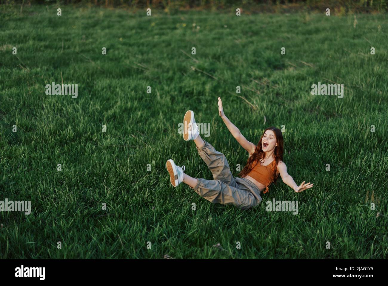 Young Woman Playing Games In The Park On The Green Grass Spreading Her Arms And Legs In