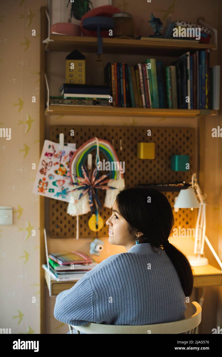 Rear view of thoughtful girl sitting at desk during studies at home Stock Photo - Alamy