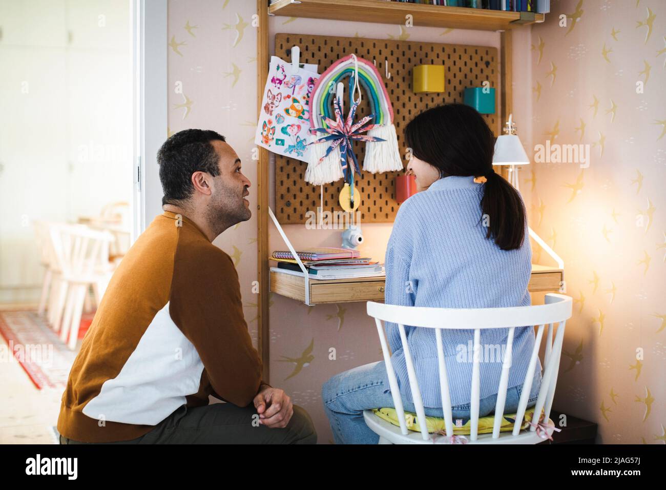 Side view of father crouching while talking with daughter sitting on ...