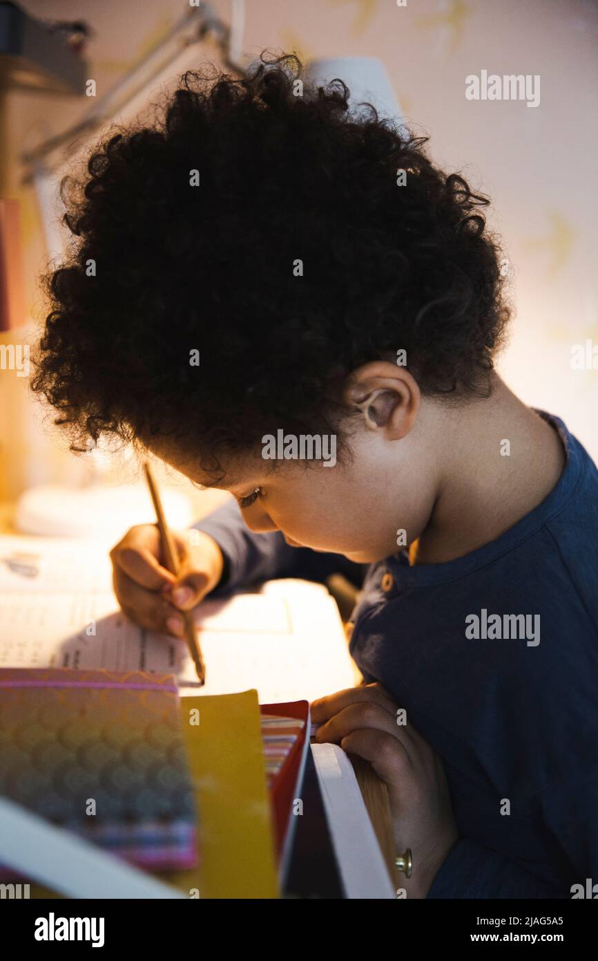 Boy with curly hair doing homework while writing in book Stock Photo ...