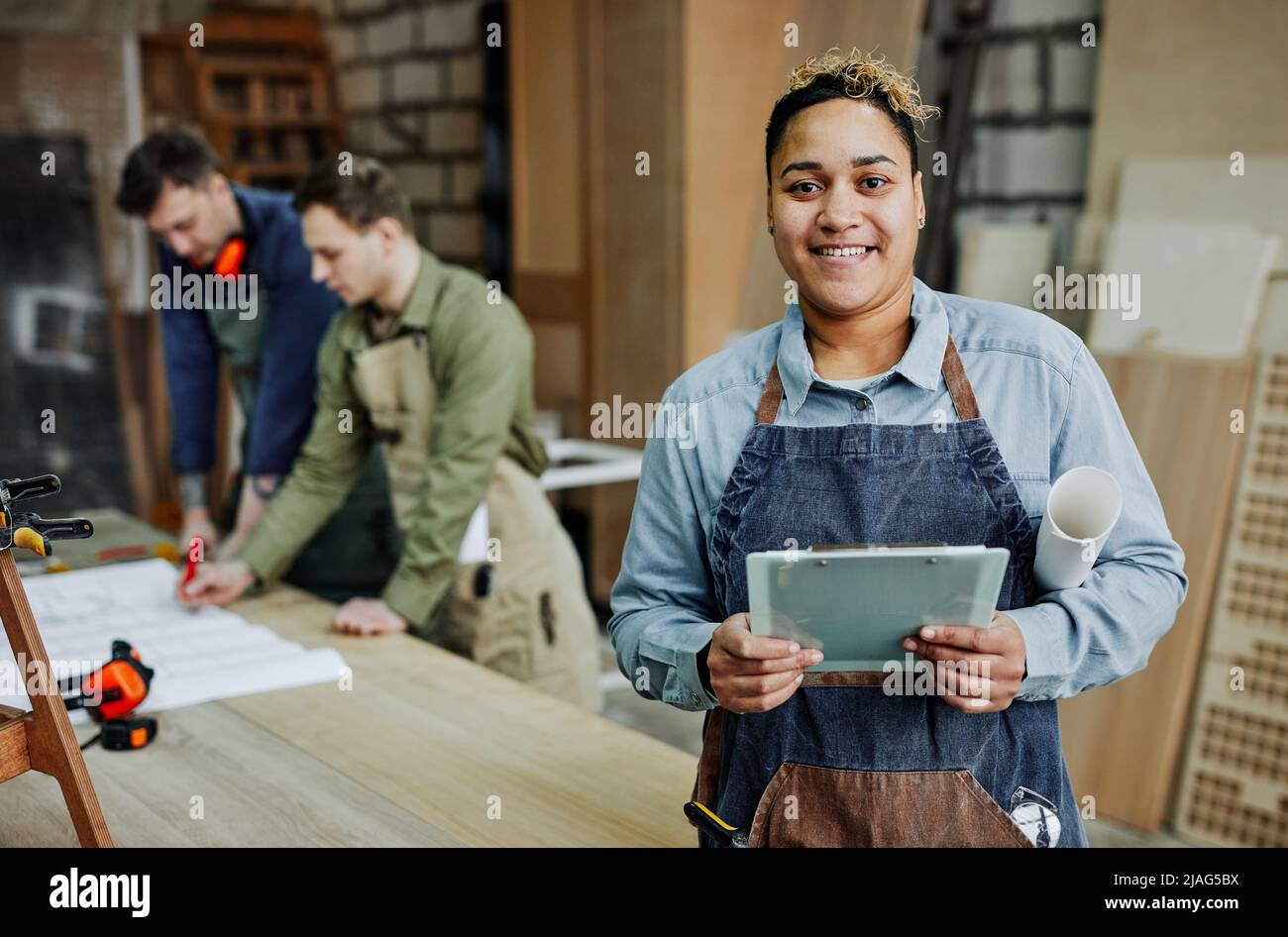 Waist up portrait of smiling female carpenter holding clipboard and ...