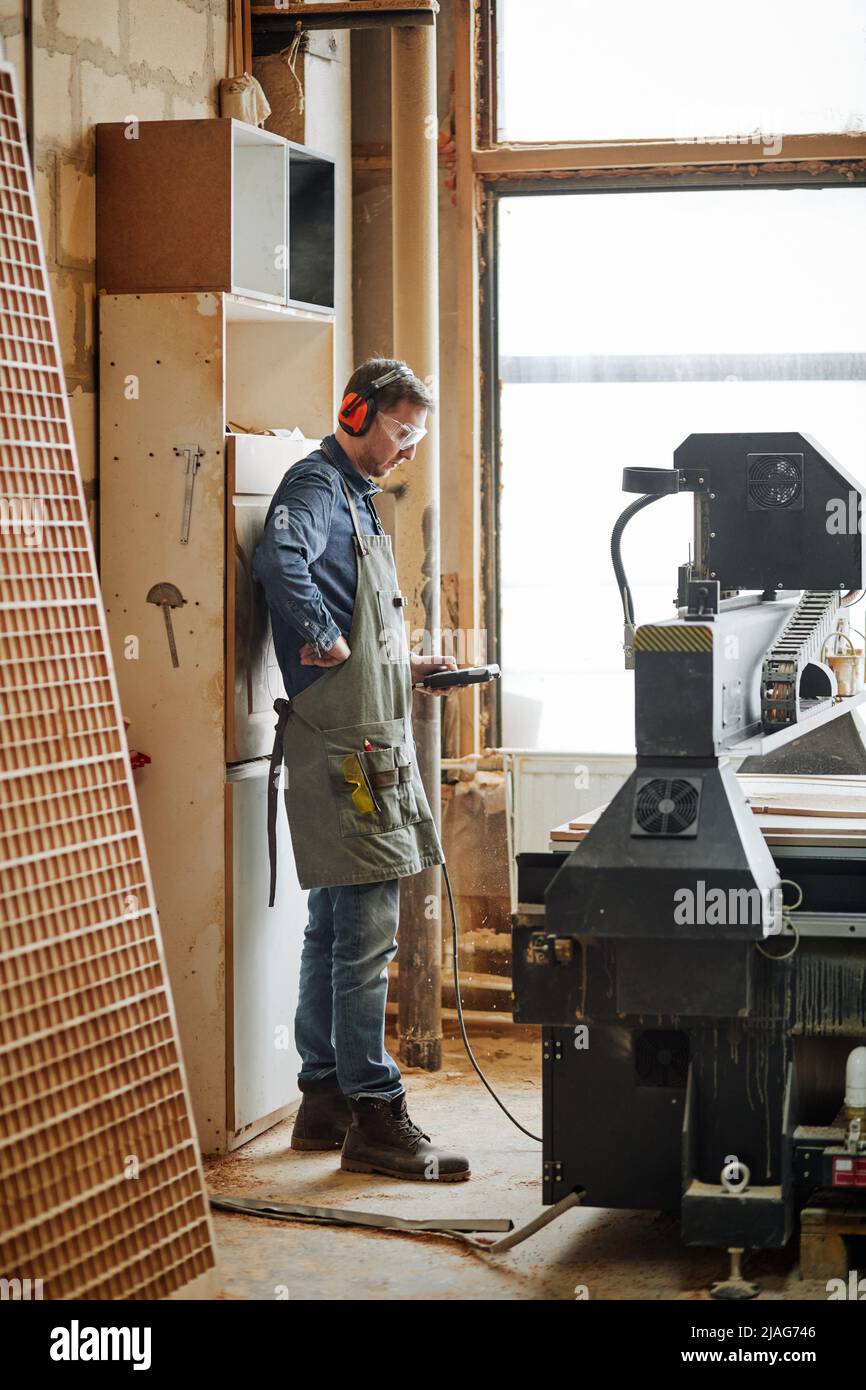 Full length portrait of male carpenter operating wood cutting machine ...