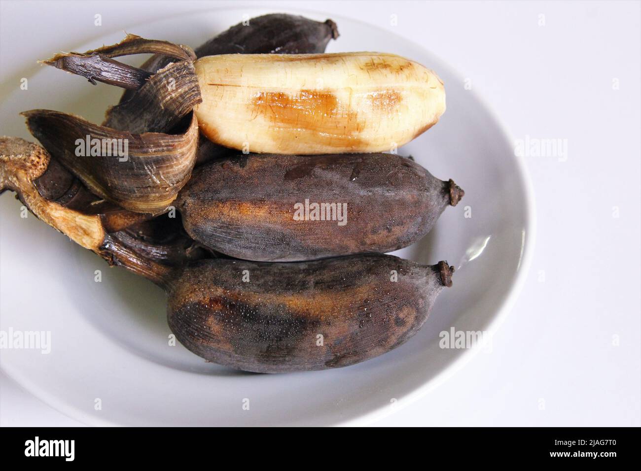 Over ripe bananas on white plate one peeled. photo isolate on white ...