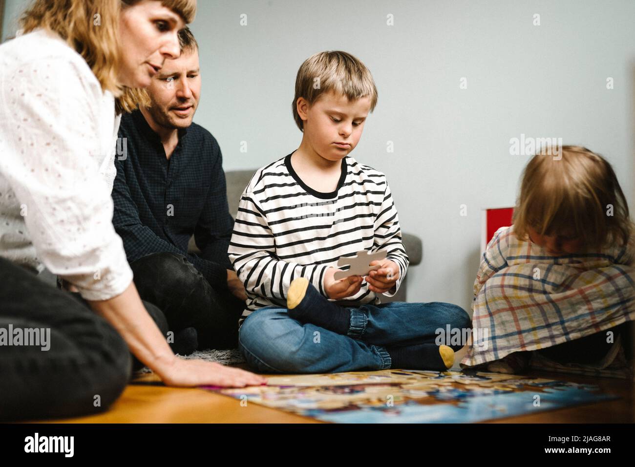 Boy having disability joining jigsaw pieces sitting with family at home ...