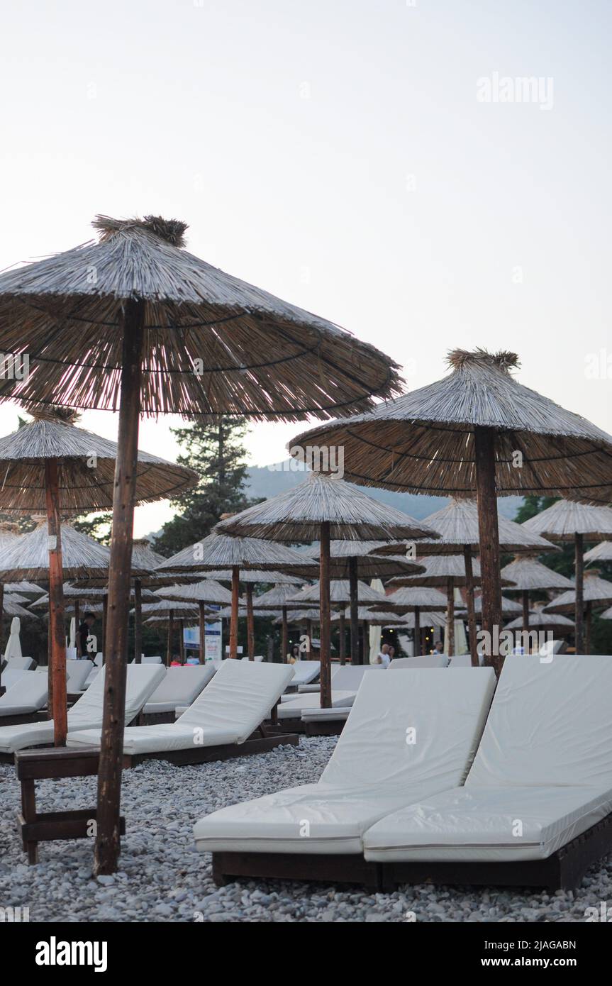 Sunbeds with straw umbrellas on the pebble beach. No people in evening ...