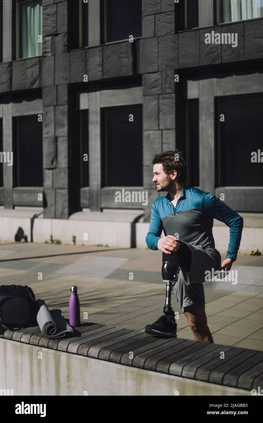 Full length of young man with disability doing stretching exercise ...
