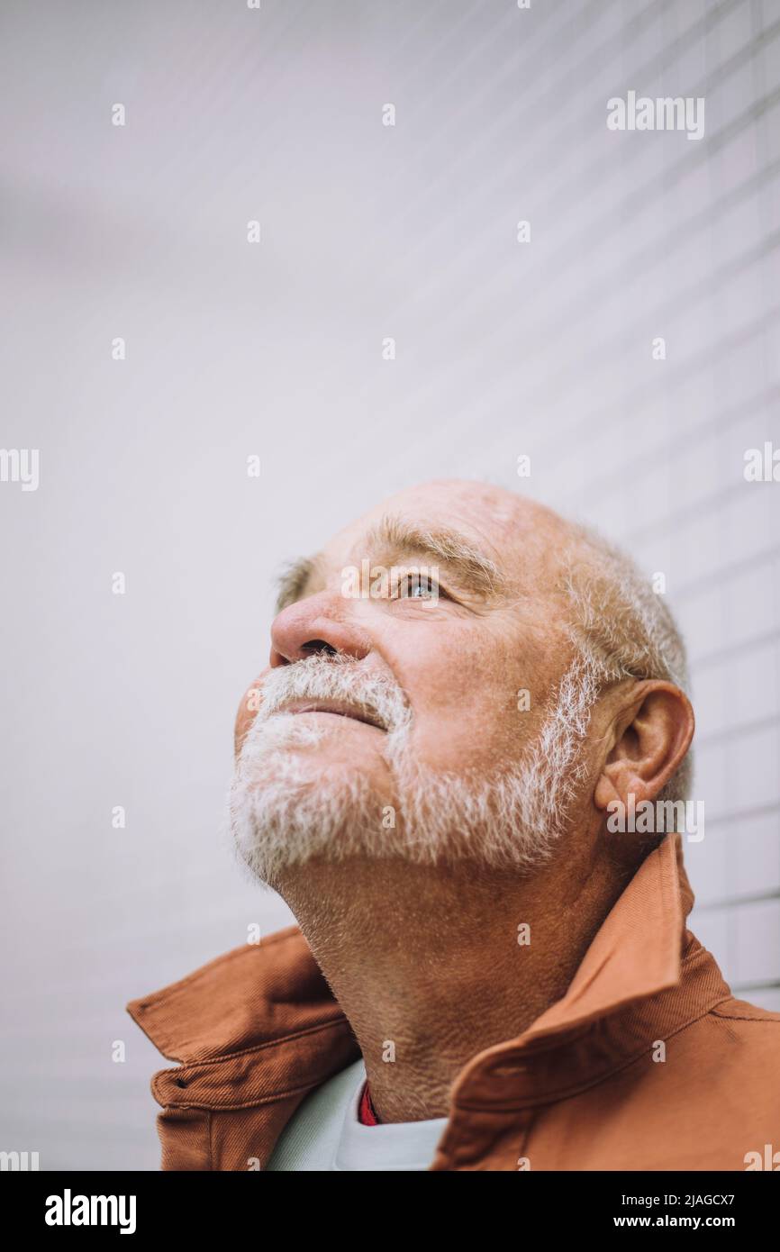 Senior man with looking up while standing against wall Stock Photo - Alamy