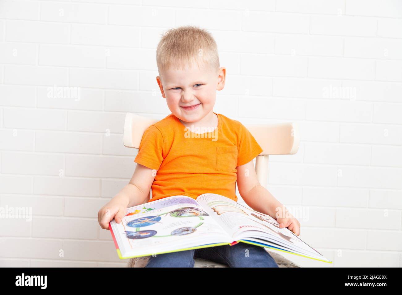 Little European boy reading a book on a chair Stock Photo - Alamy