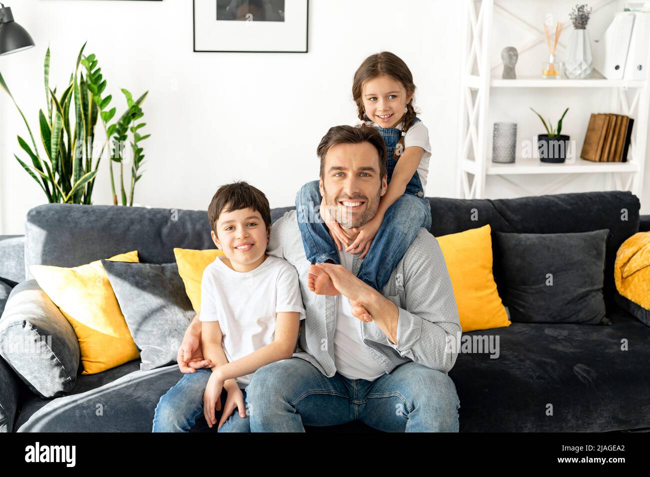 Portrait of cheerful multiracial family -dad, son and toddler daughter sitting on the sofa in ...