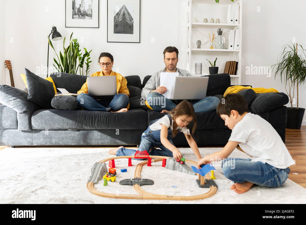 Parents work remotely with laptops sitting on the couch in living room ...
