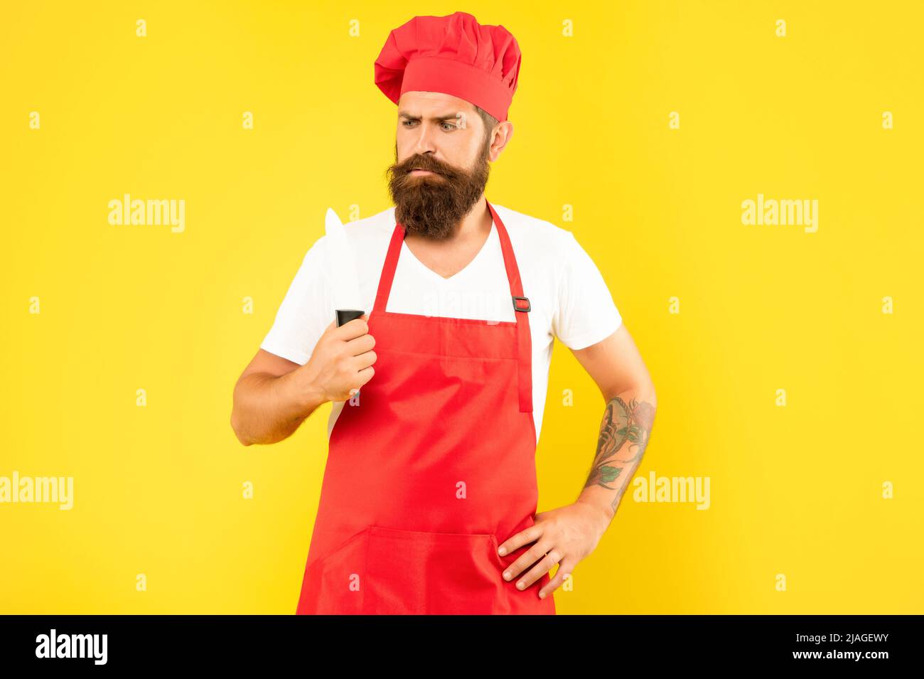 Frown man in red apron and toque looking at chefs knife in hand yellow ...