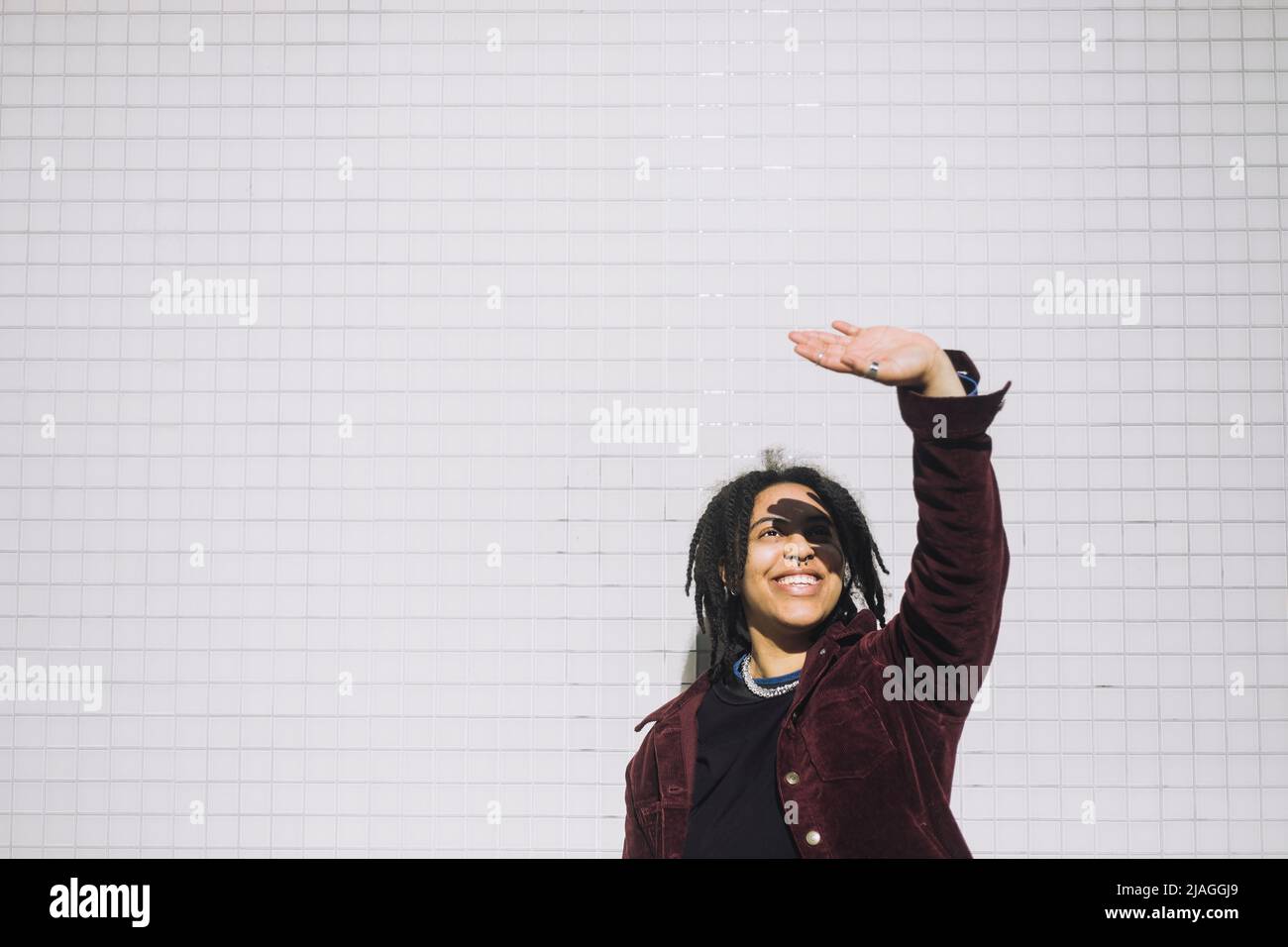 Happy genderqueer person shielding eyes while standing against wall ...