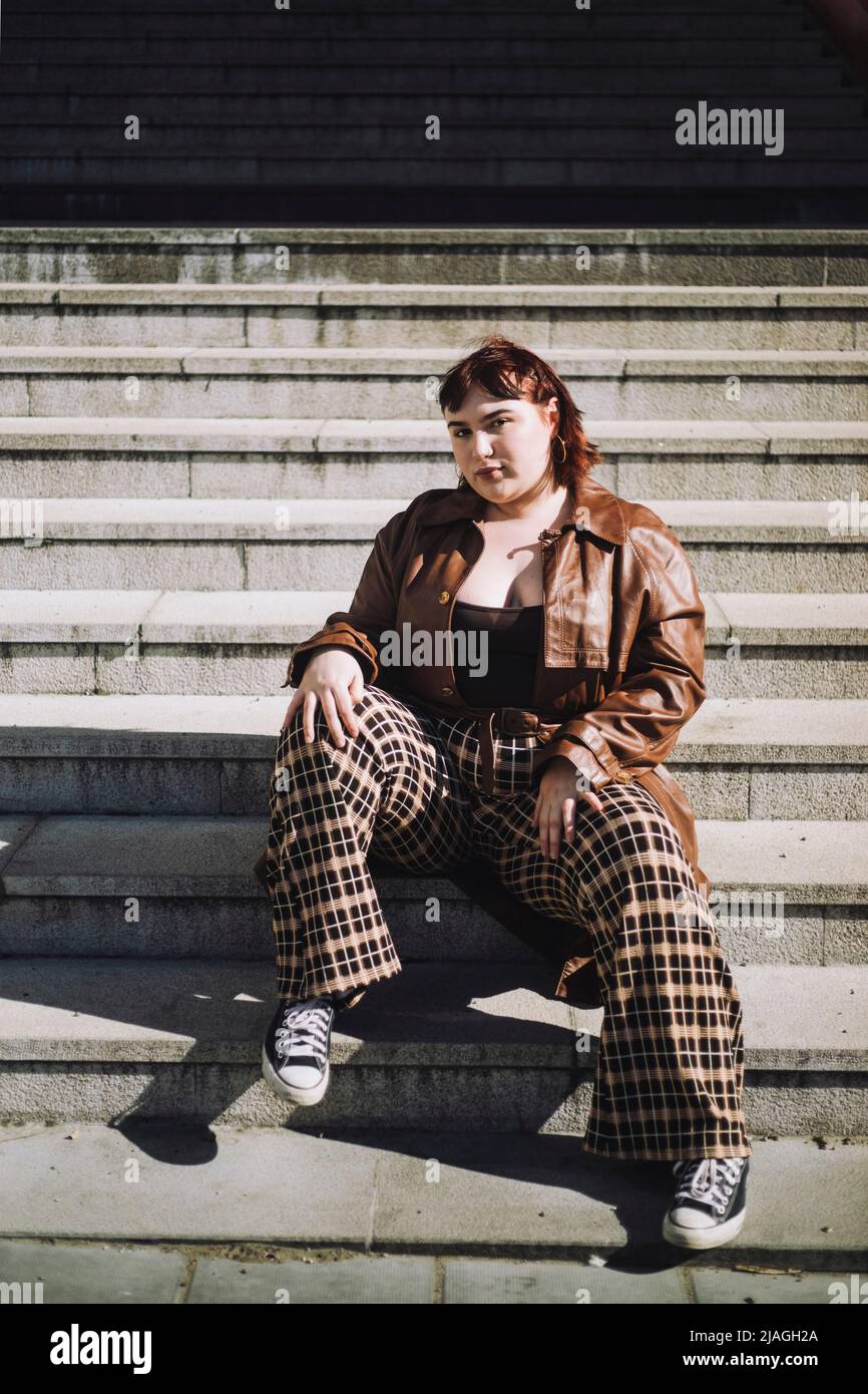 Portrait of confident young woman sitting on steps during sunny day ...