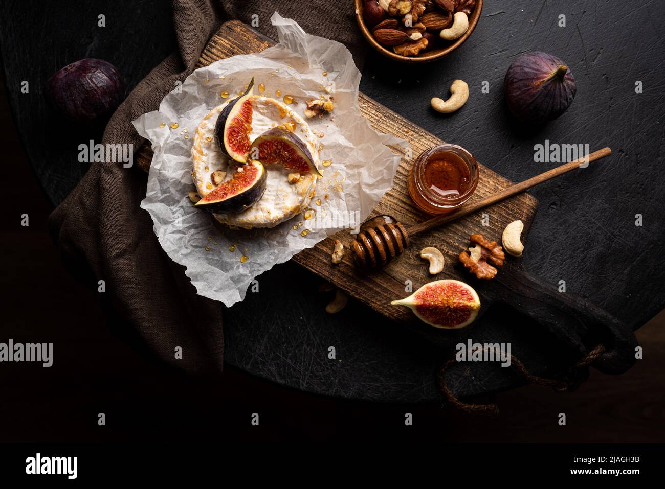 Brie cheese on a wooden Board with fresh figs and honey over dark table ...