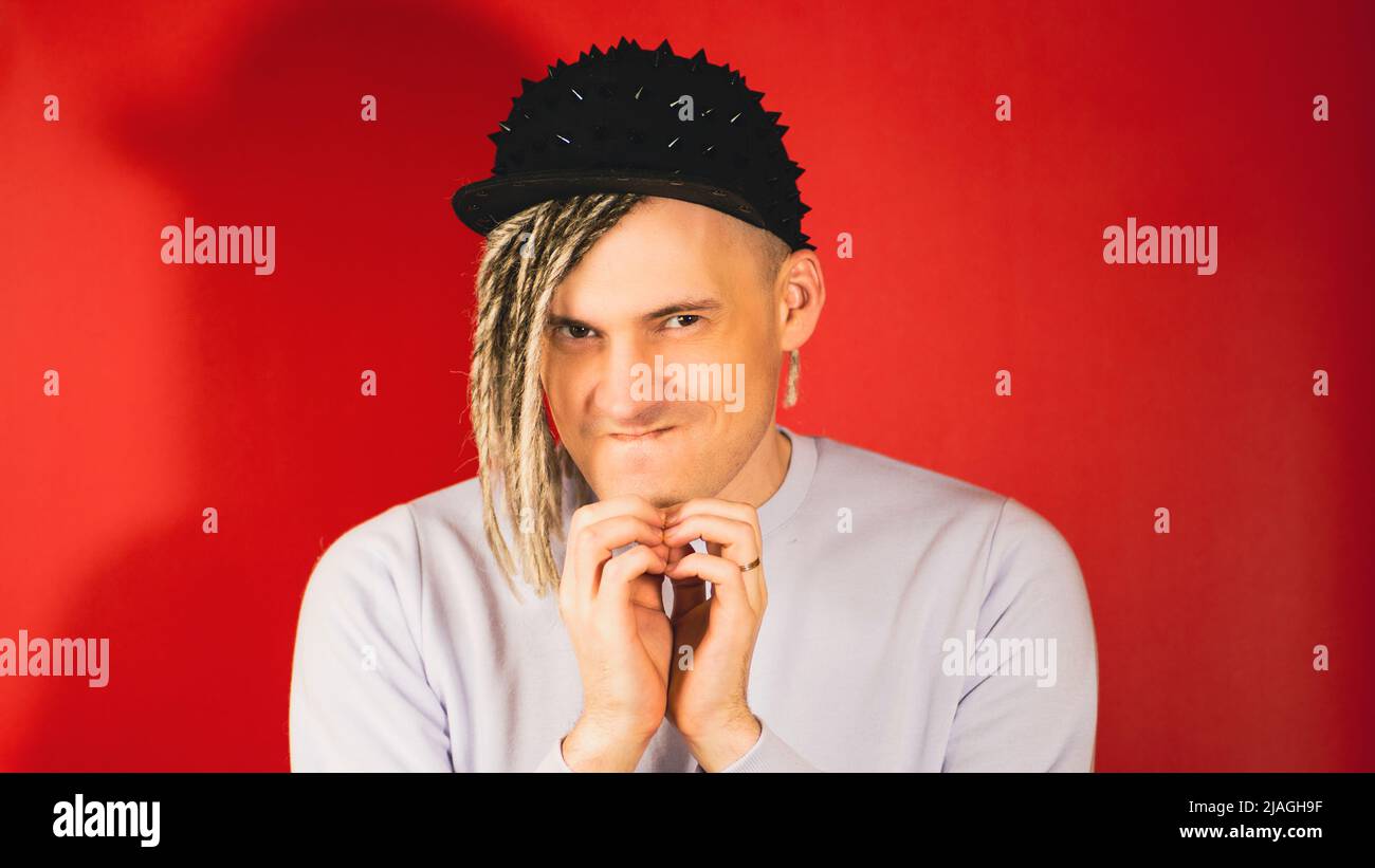 Young handsome sly man with blonde dreadlocks in black cap looking at ...