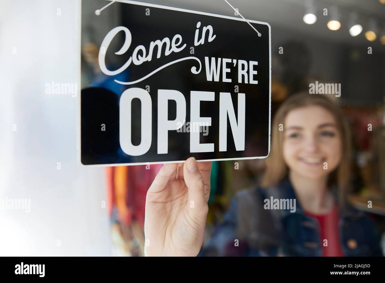 Smiling Female Owner Of Small Business Turning Round Open Sign In Shop ...