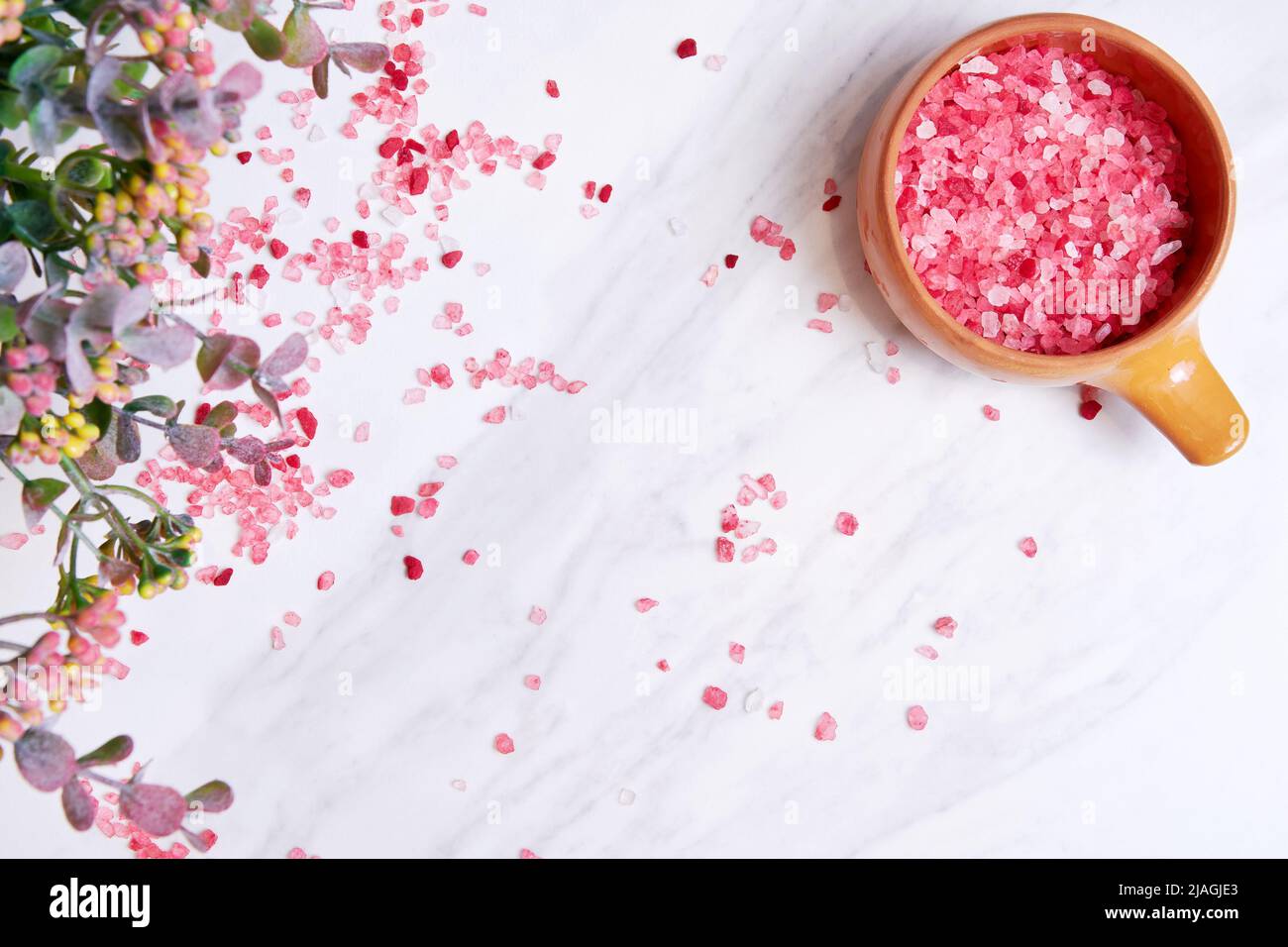 Scattered pink bath salt grain on the marble surface with flowers and ...