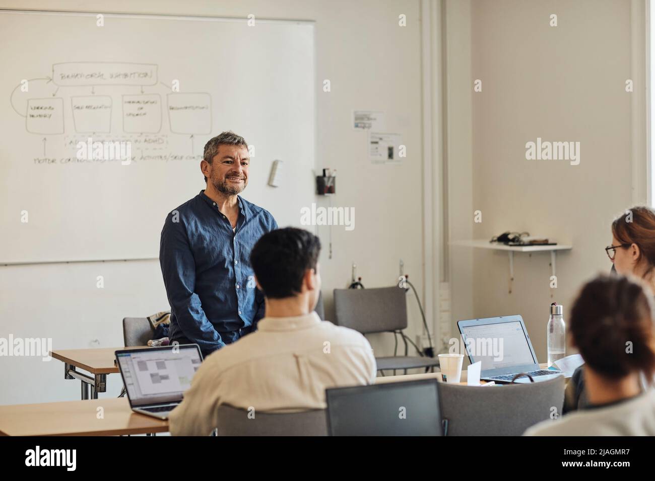 Smiling male professor looking at students in classroom Stock Photo - Alamy