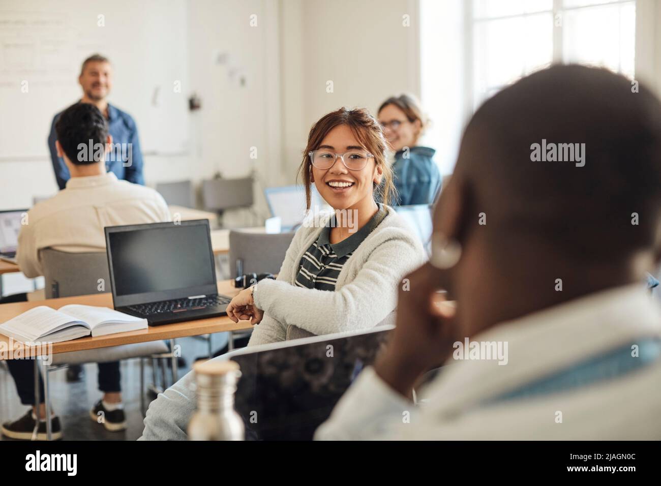 Smiling female student talking to male friend during lecture in ...