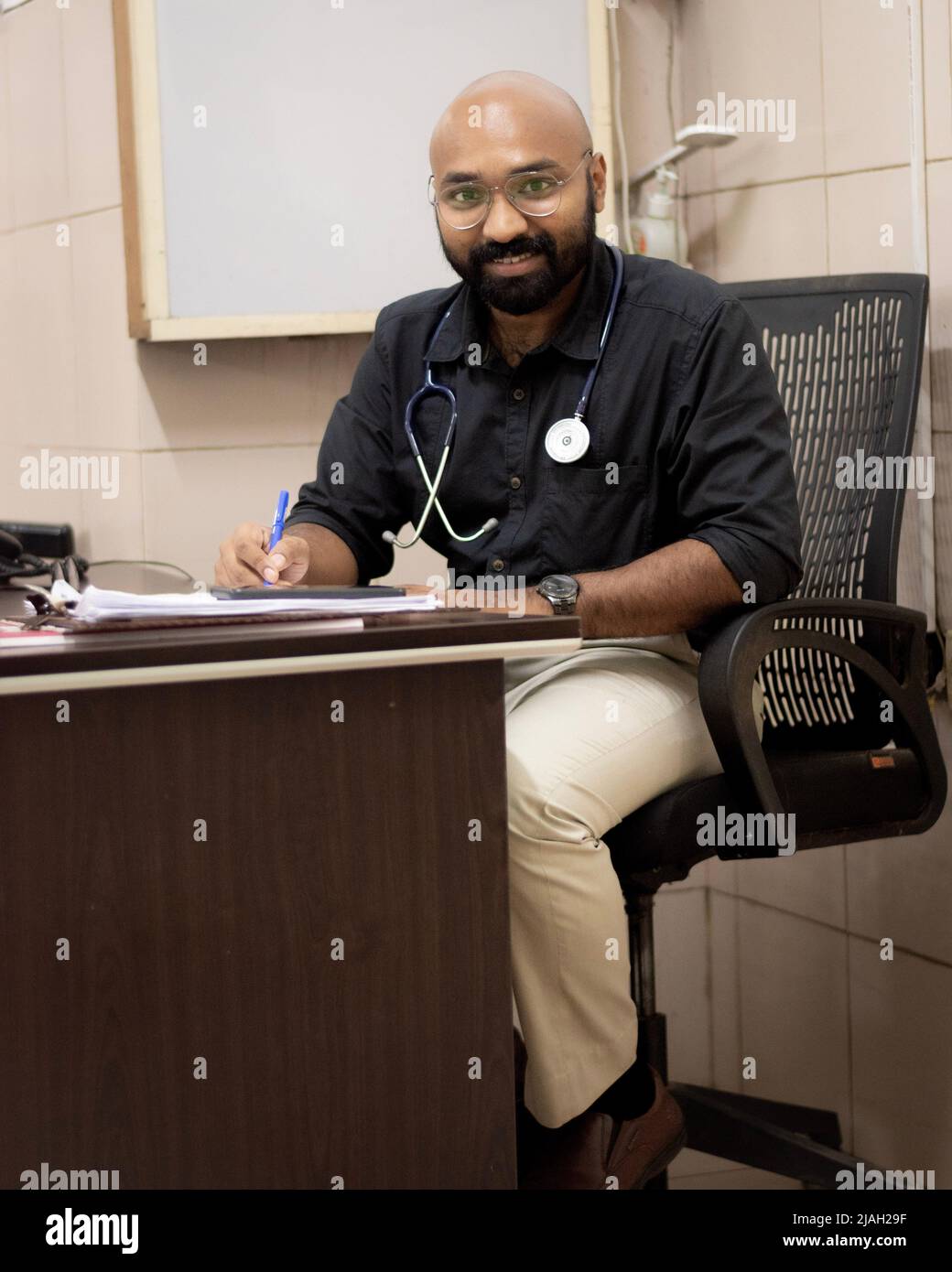 A picture of an Indian doctor sitting in his clinic chair with a ...