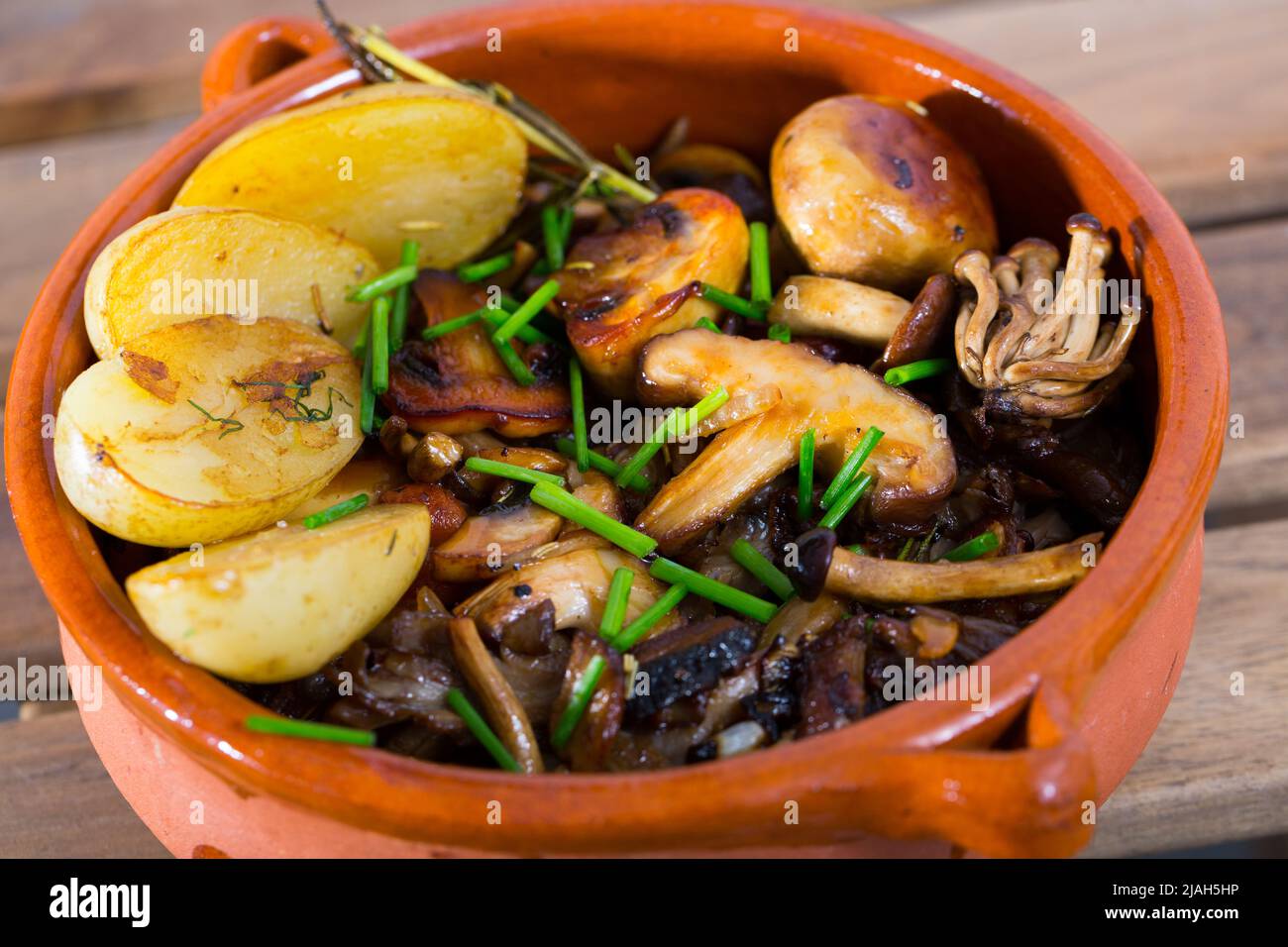 Tasty different mushrooms cooked at clay pot with potatoes at table ...