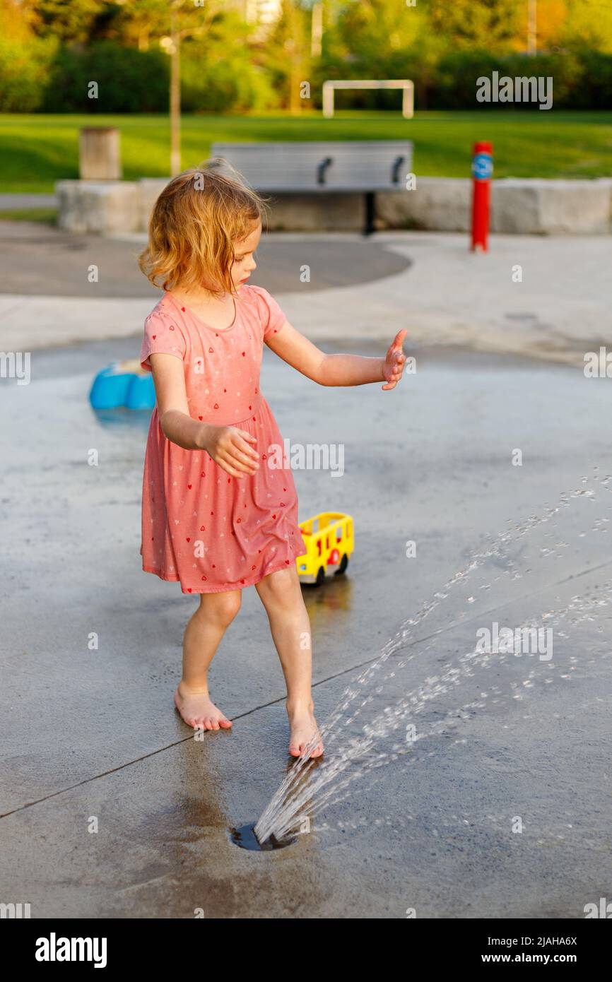 Little girl playing in park with fountains in summer. Small child ...