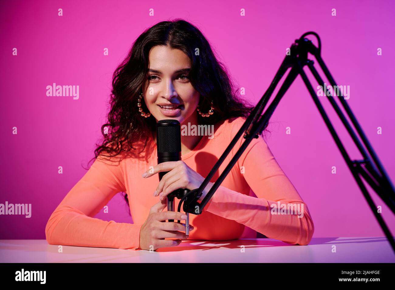 Beautiful young female influencer sitting at desk in studio in pink ...