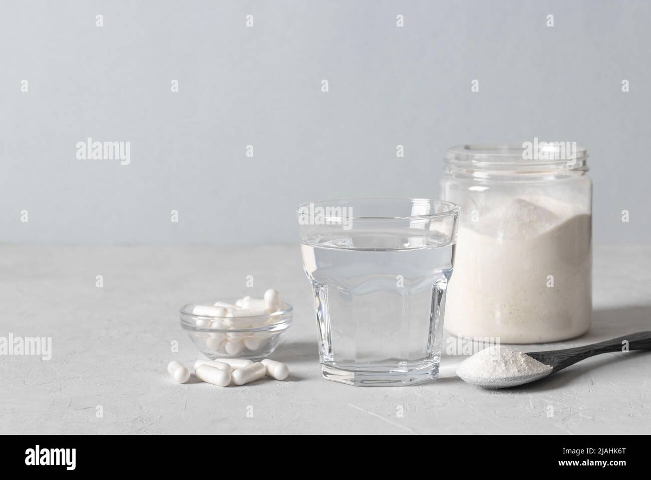 Collagen powder in spoon, collagen capsules, glass of water and jar of ...