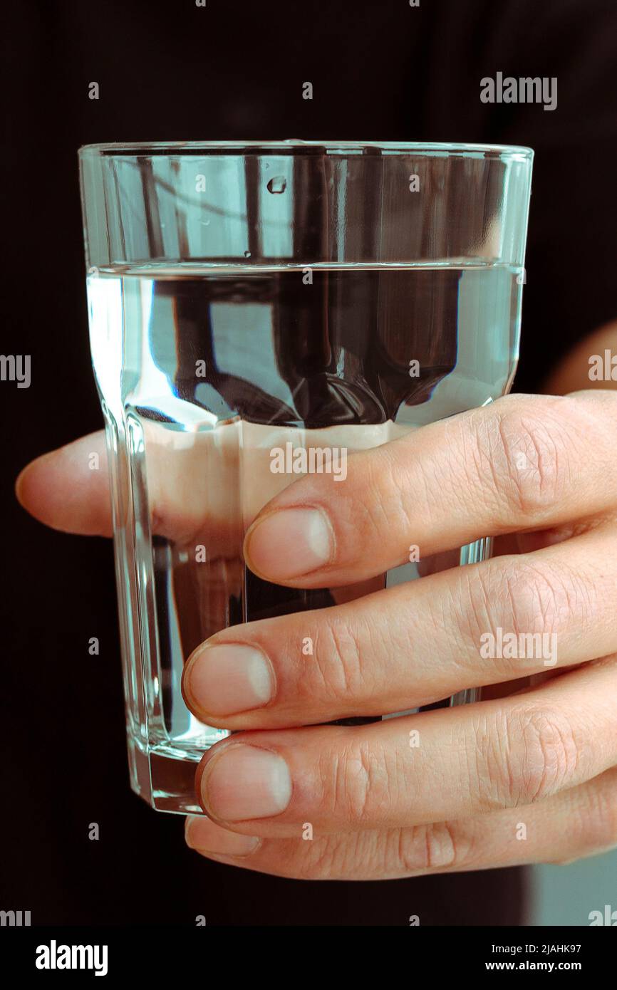 A glass with clean melted water in the hand of a man Stock Photo - Alamy
