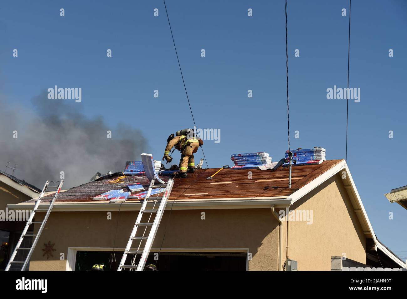 SDFD Firefighter moves shingles away from seat of the fire at a ...