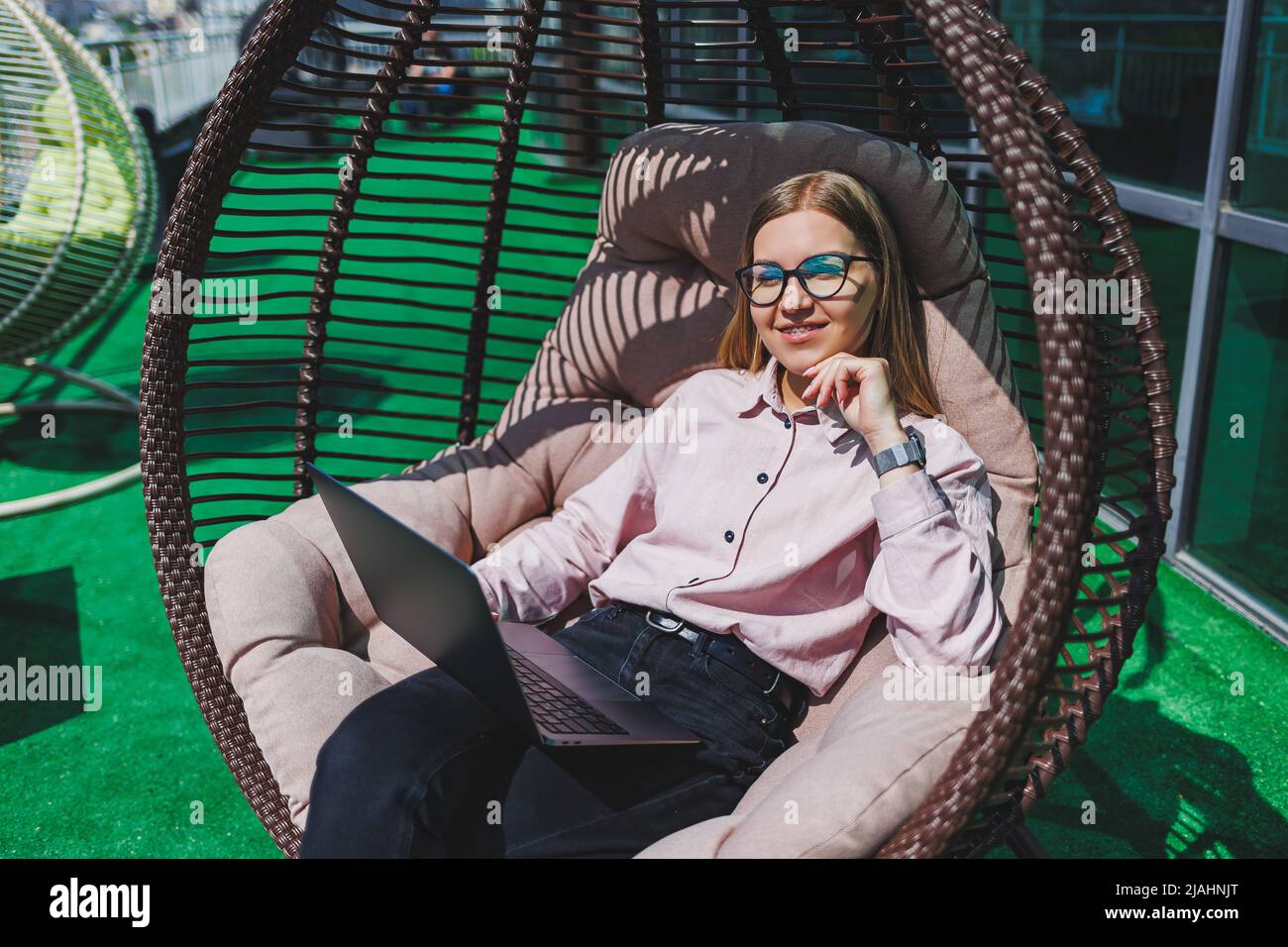 Attractive woman sits with a laptop on the balcony and works, looking ...