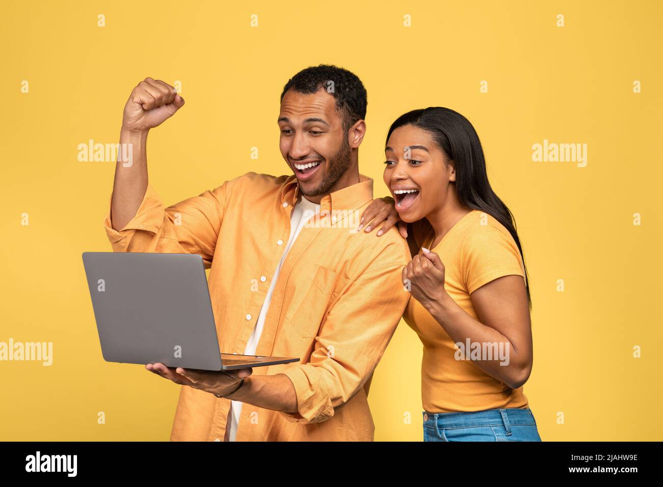 Millennial black couple making YES gesture, looking at laptop ...