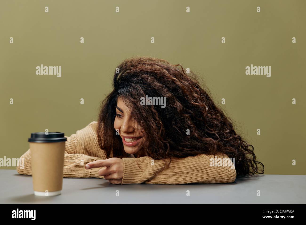 Enjoyed smiling happy tanned curly Latin female look at coffee cup to ...