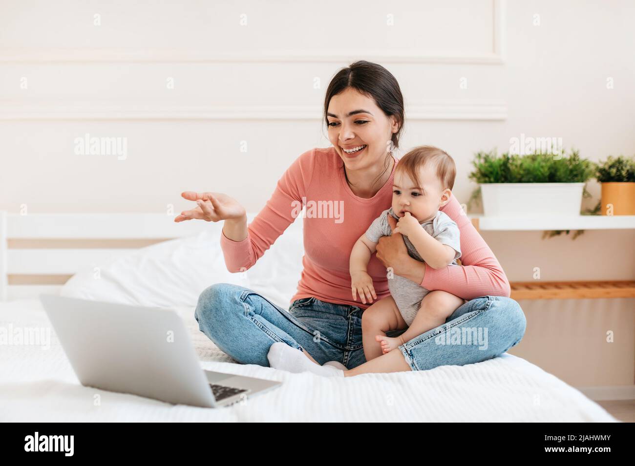 Excited mother holding baby and making video call with laptop, sitting ...