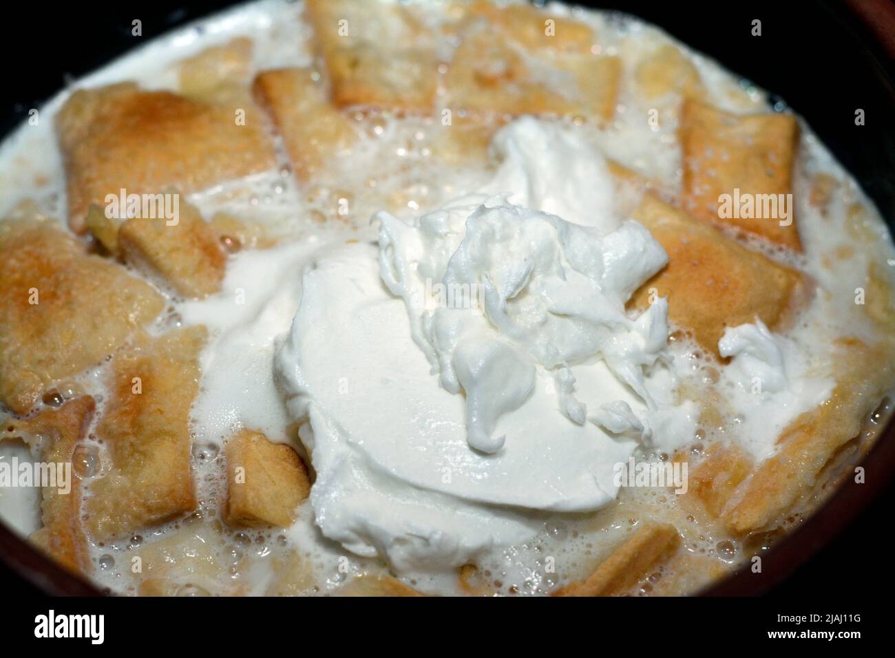 whipped cream on top of Egyptian bread pudding, milk in a brown bowl ...