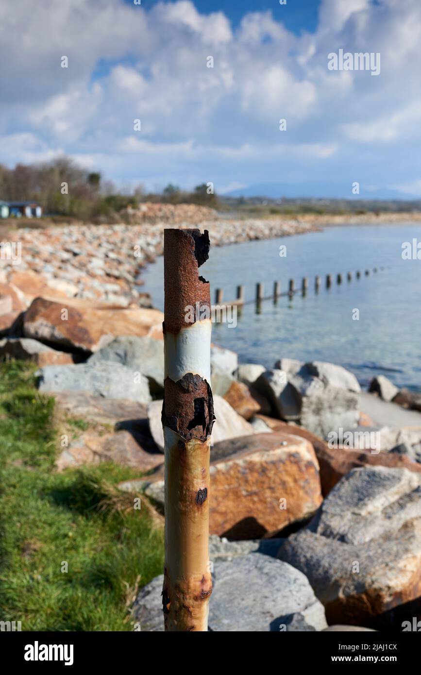 Damaged Steel pole with rust and corrosion, and blurred rock armour sea ...
