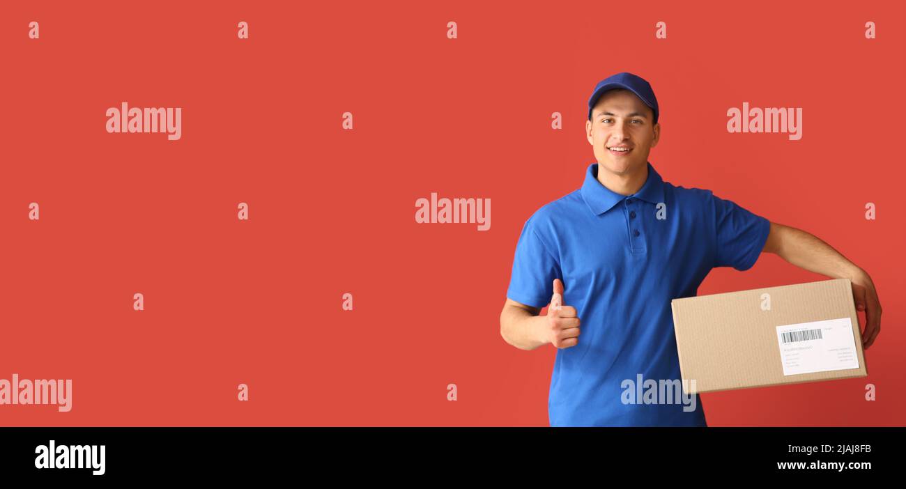 Delivery man holding parcel and showing thumb-up on red background with ...