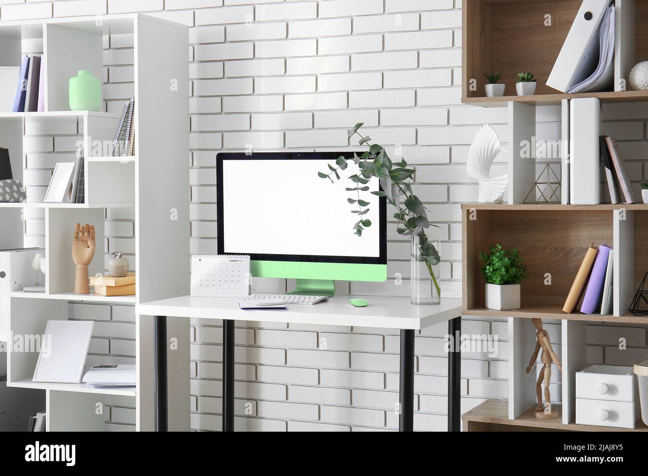 Workplace with modern computer and shelving units near white brick wall ...