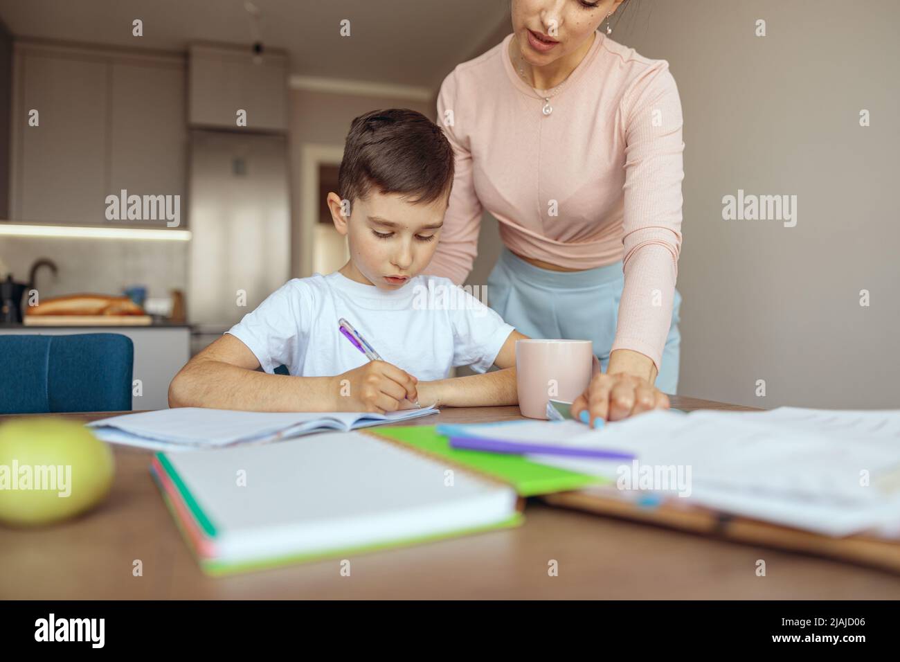 Caucasian little teen boy sitting at table and writing exercise in ...