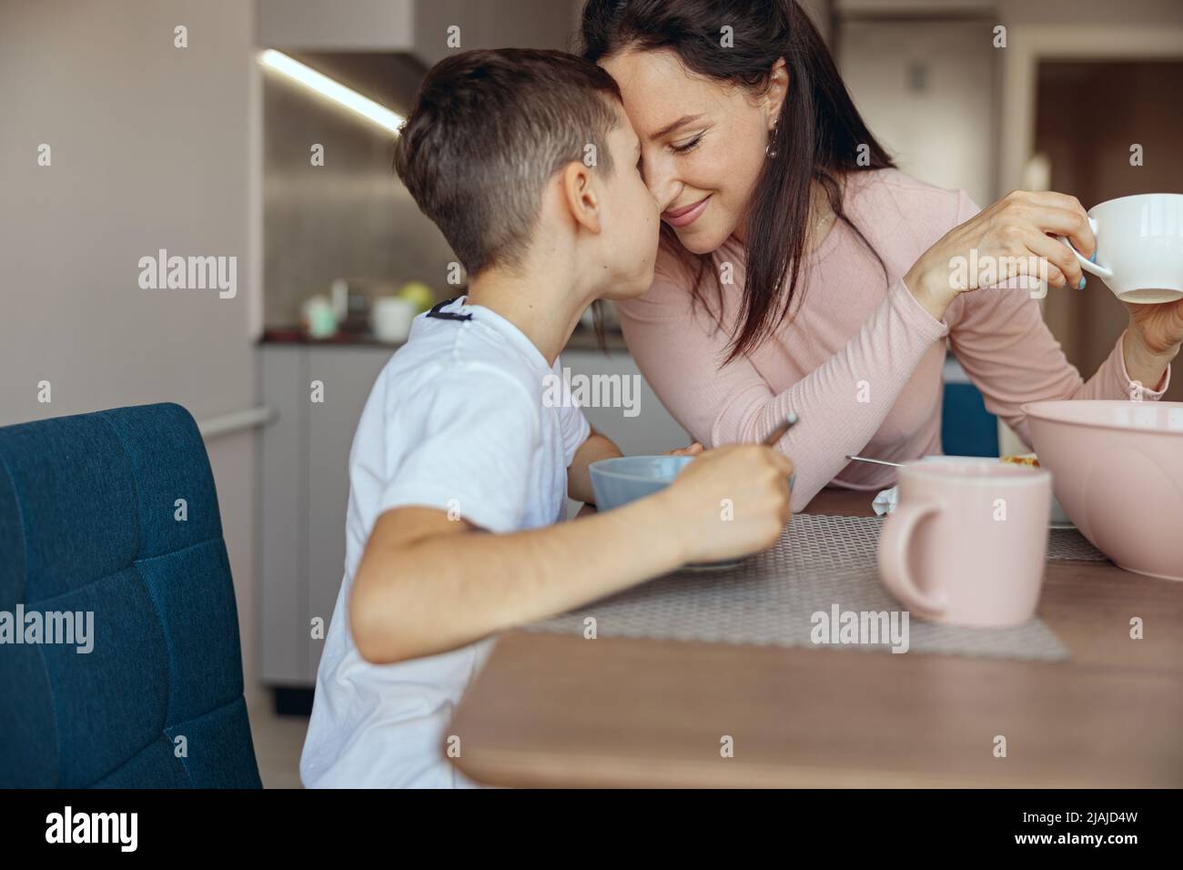 Happy mother and small teen son cuddling nose to nose in kitchen while ...