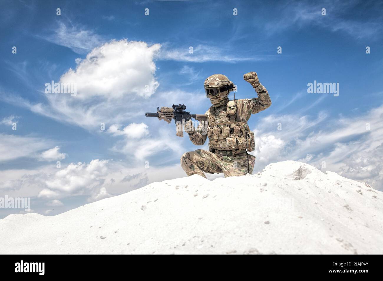 Soldier armed with assault rifle, kneeling on top of a sand dune ...
