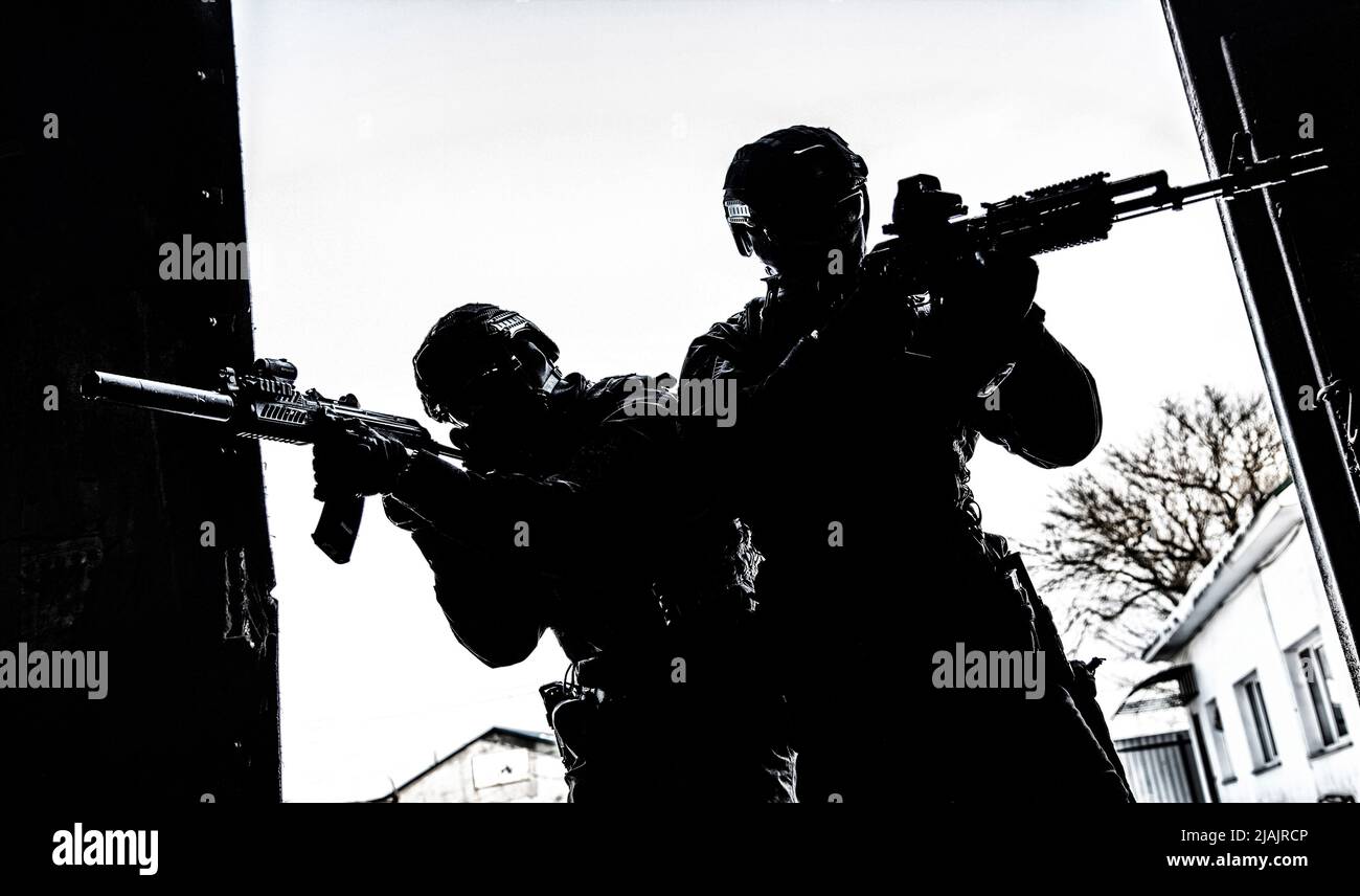 Silhouettes of SWAT team members aiming assault rifles while standing ...
