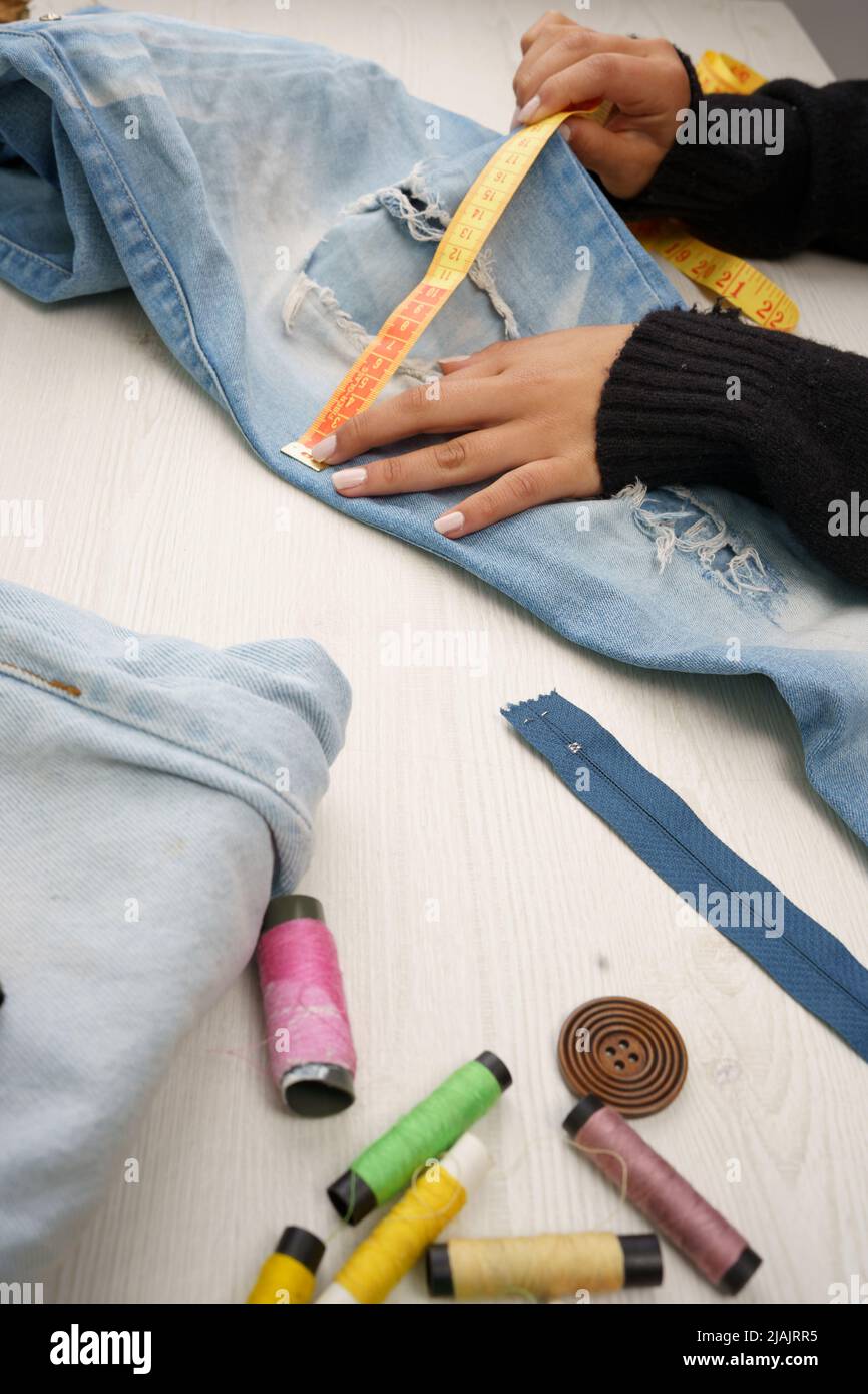 working in a sewing workshop measuring to repair a jeans fabric with a ...