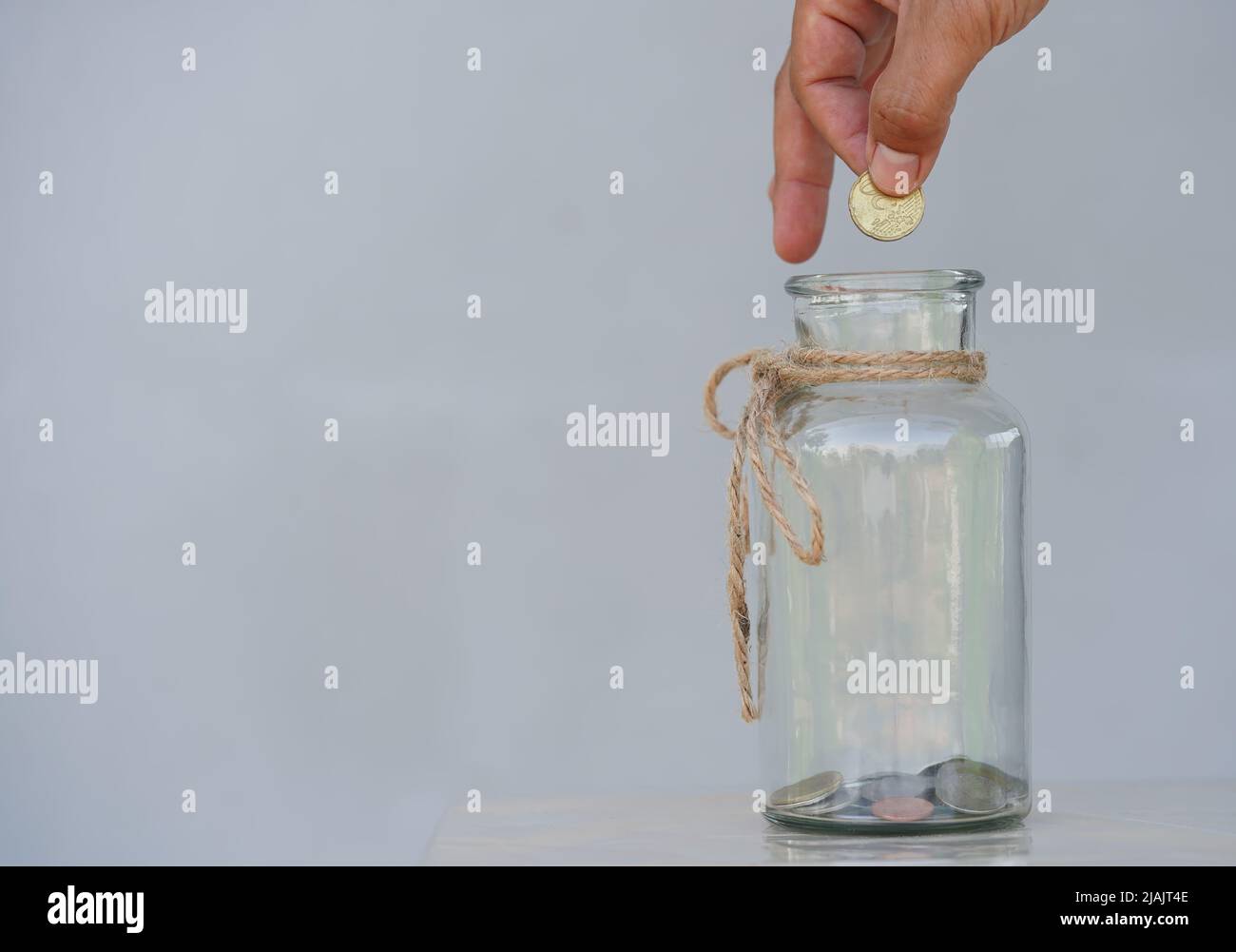 Hand putting coin in a glass jar with coins on white background ...