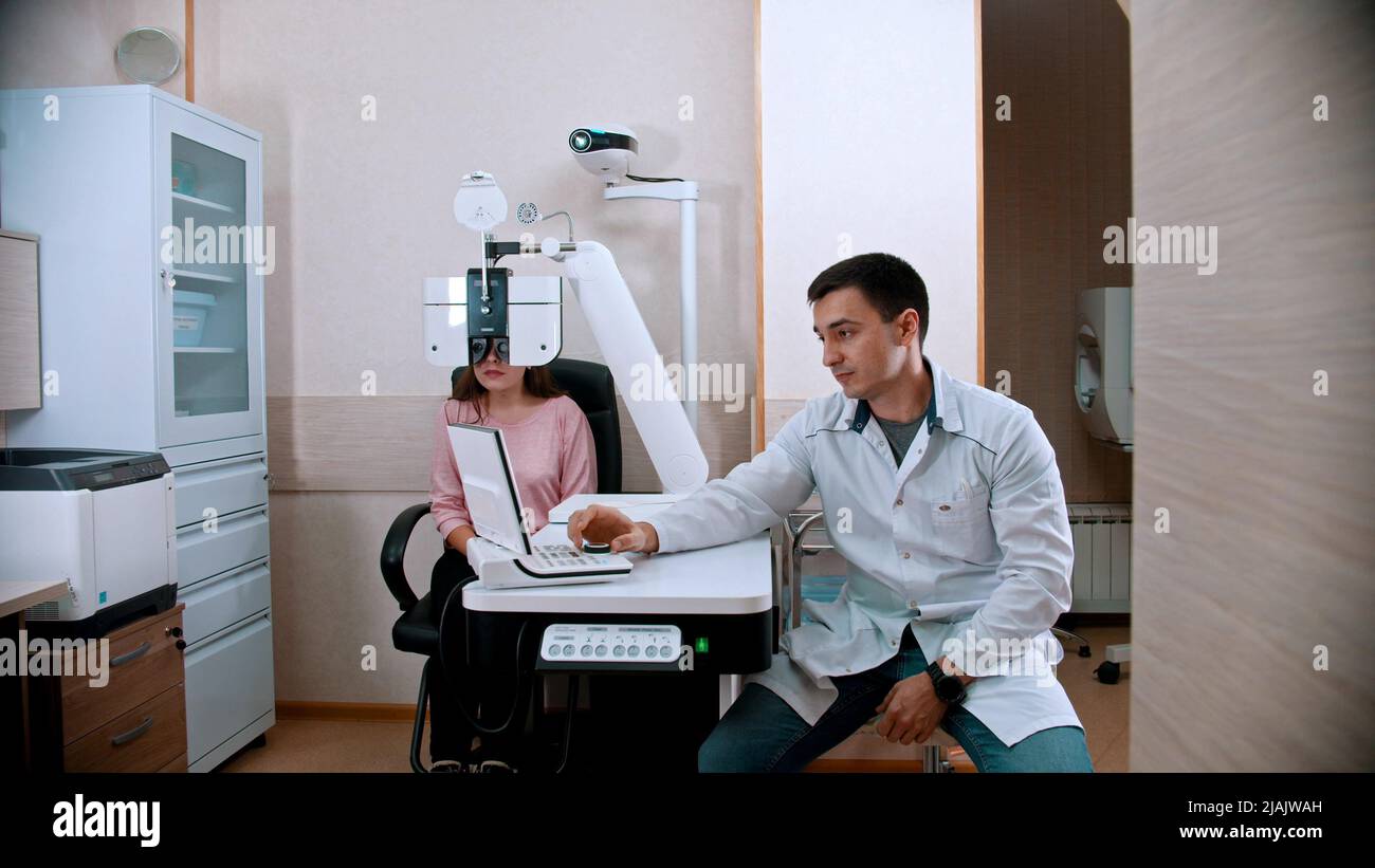 Ophthalmology treatment - young woman checking her visual acuity with an optometrist equipment ...