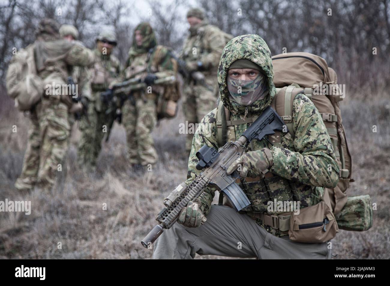 Infantry soldier wearing hooded camo jacket and backpack, kneeling with ...