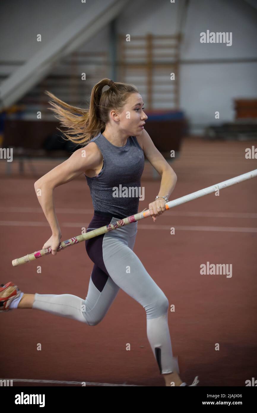 Pole vaulting indoors - young fit woman running with a pole in the ...