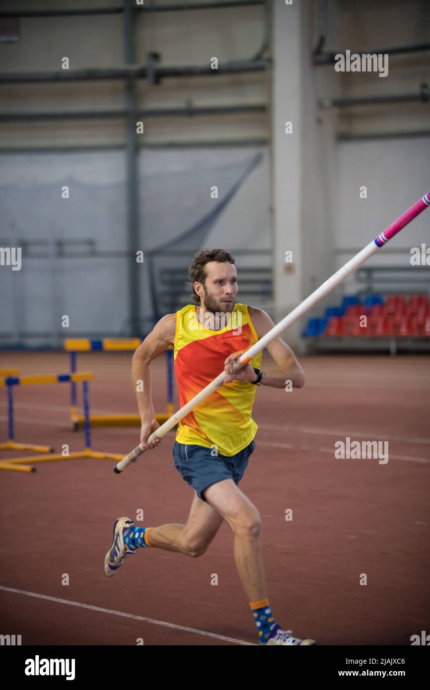 Pole vaulting indoors - a man running on the track with a pole in the ...