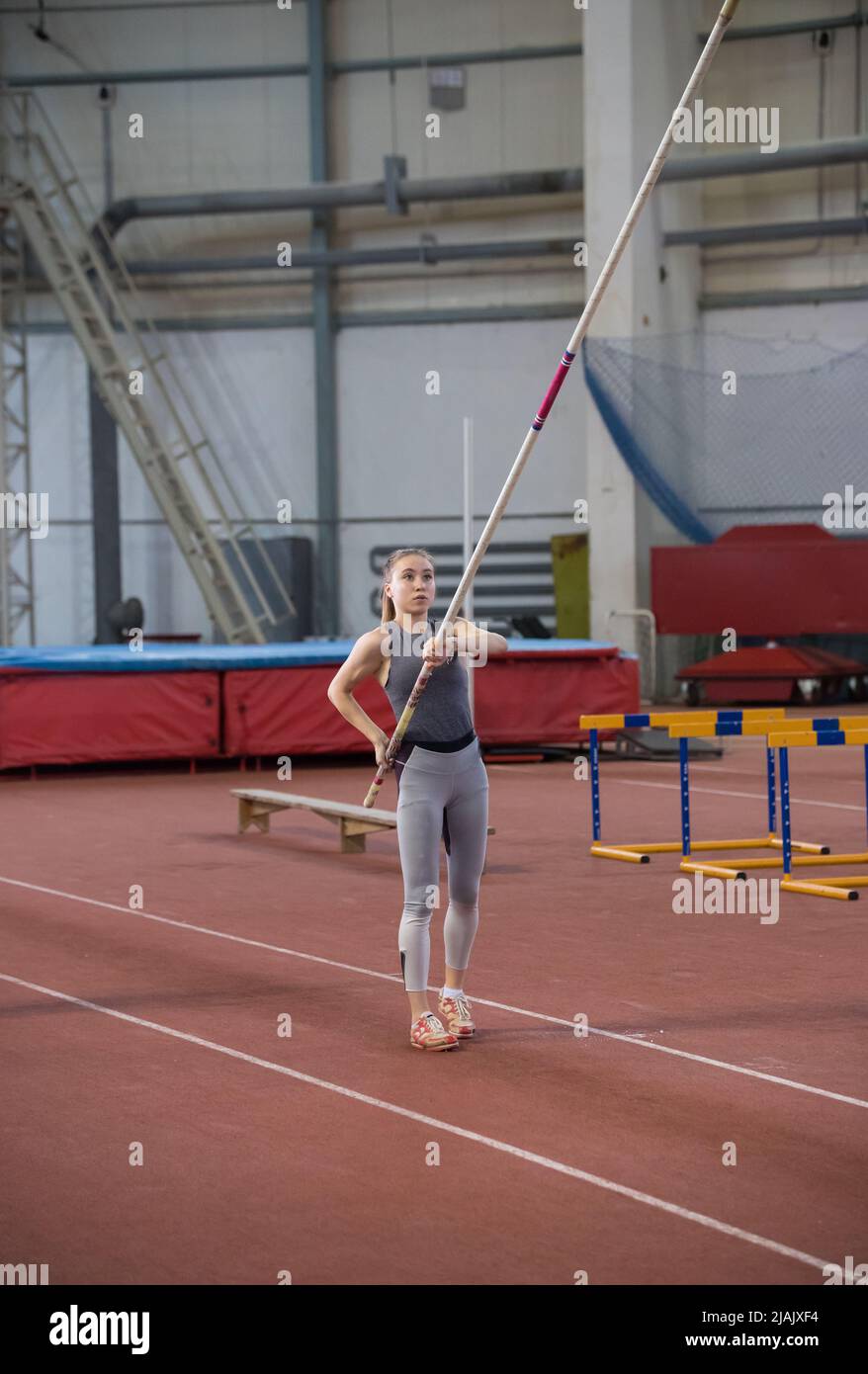 Pole vaulting indoors - young woman holding a pole looking up on it ...