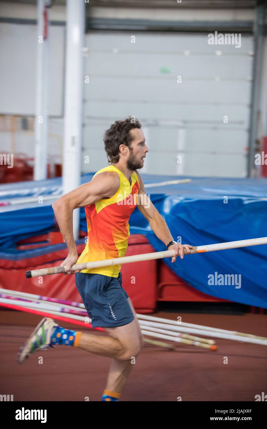 Pole vaulting indoors - a athletic man running on the track with a pole ...